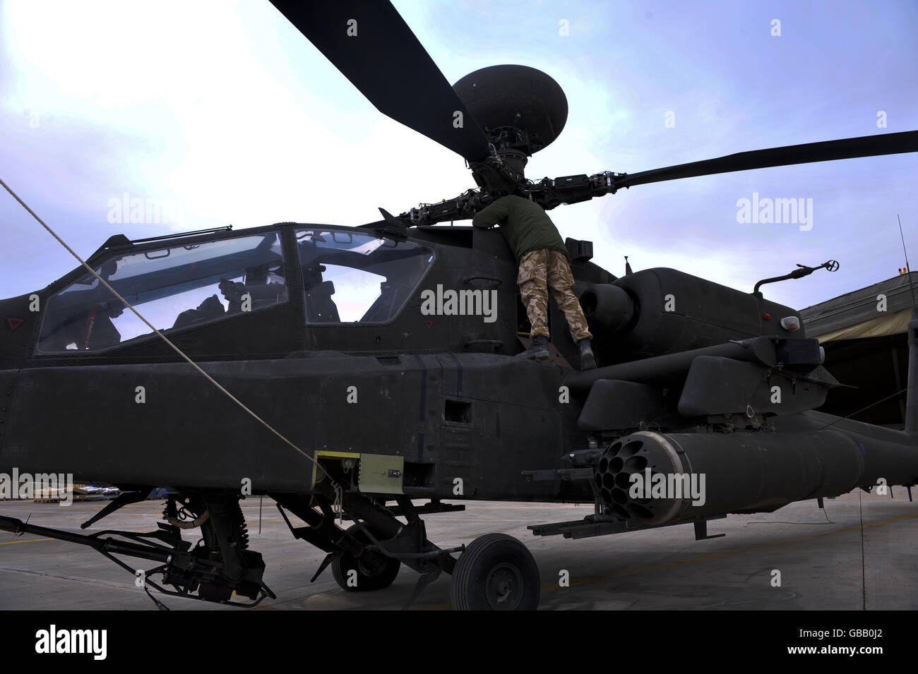 An Apache helicopter is checked over by a mechanic as it rests on the ...