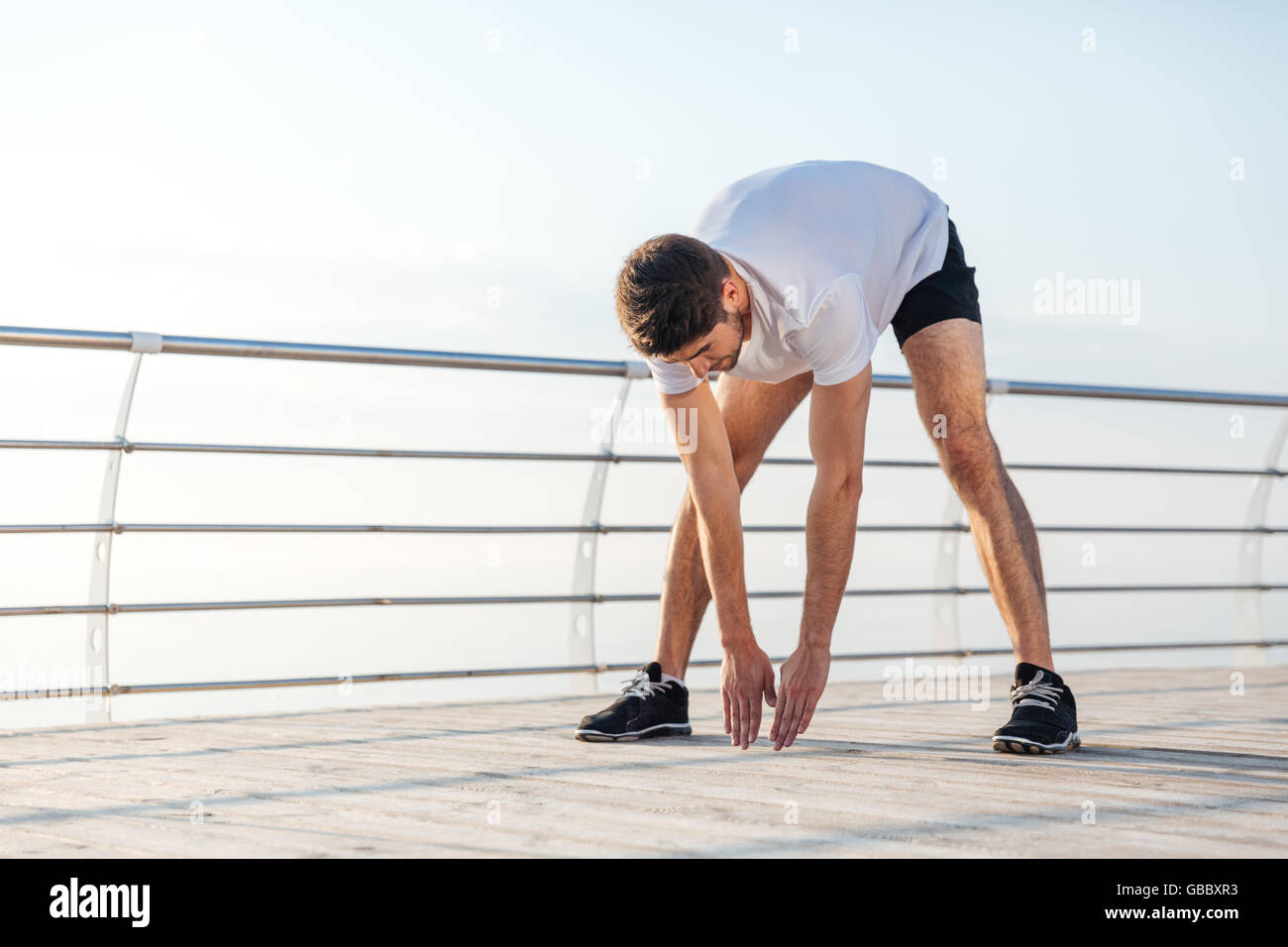 Confident young male athlete stretching and warming up before jogging ...