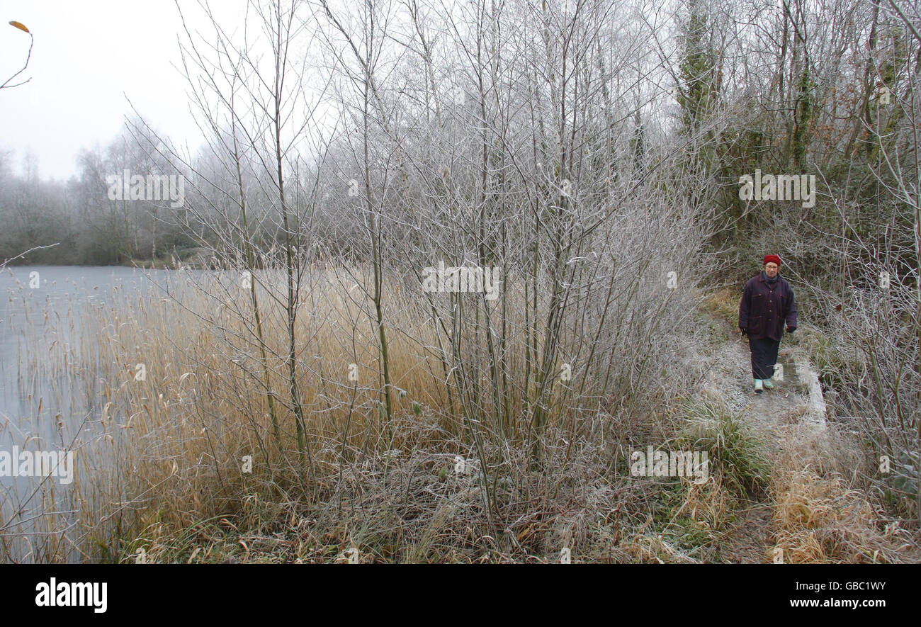 A woman takes a walk through a frosty scene by a frozen lake at ...