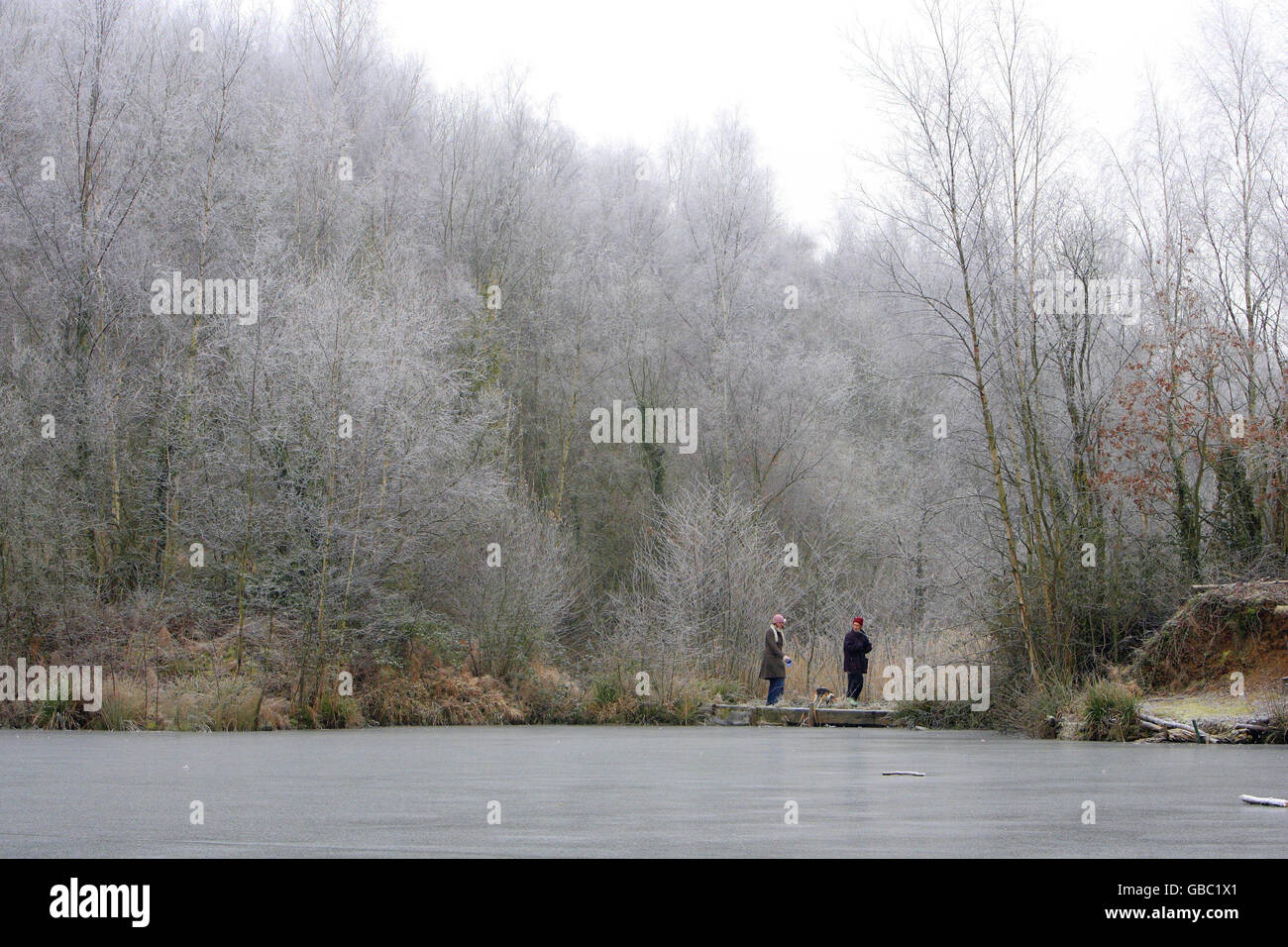 A couple take a walk through a frosty scene by a frozen lake at ...