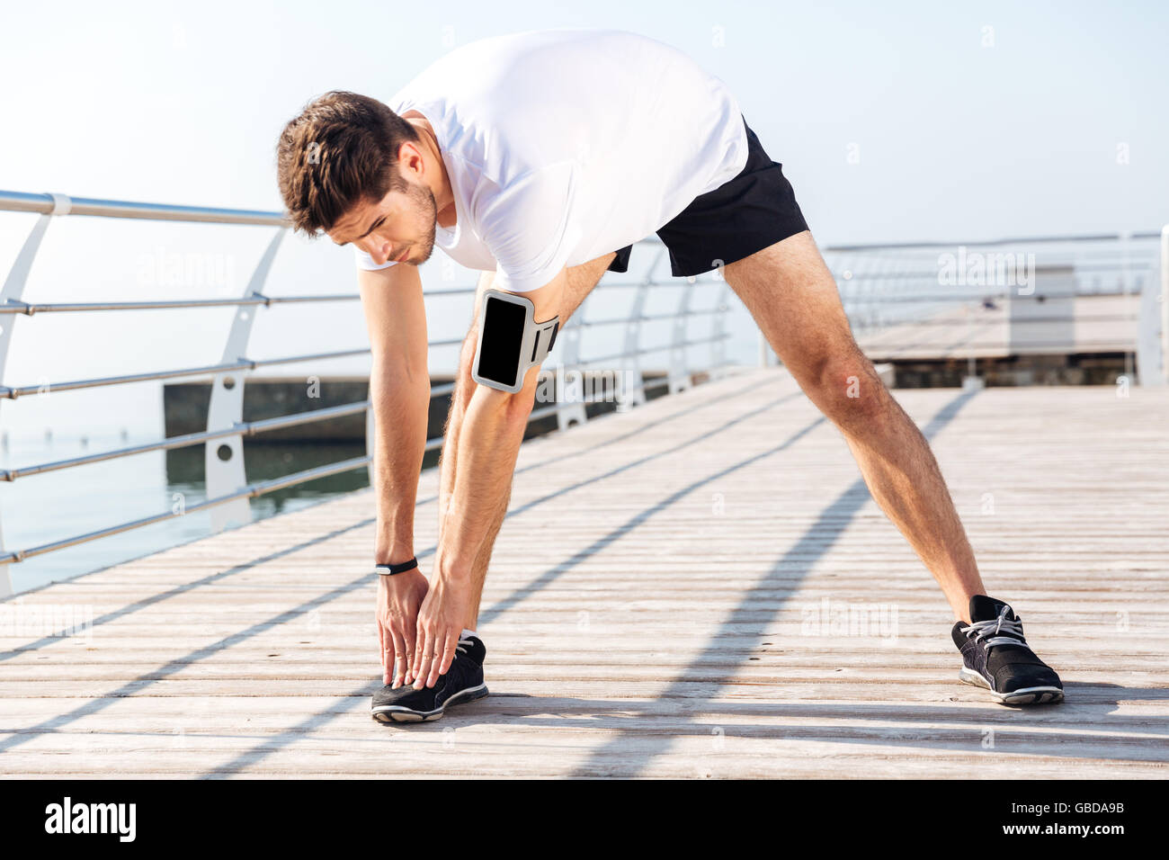 Handsome young sportsman stretching legs during workout on pier Stock ...