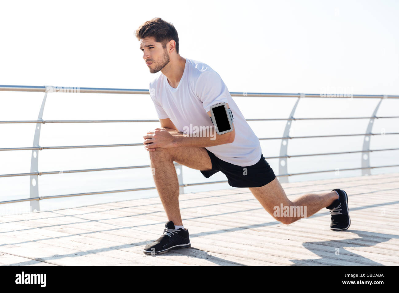 Handsome young sportsman stretching legs during workout on pier Stock ...