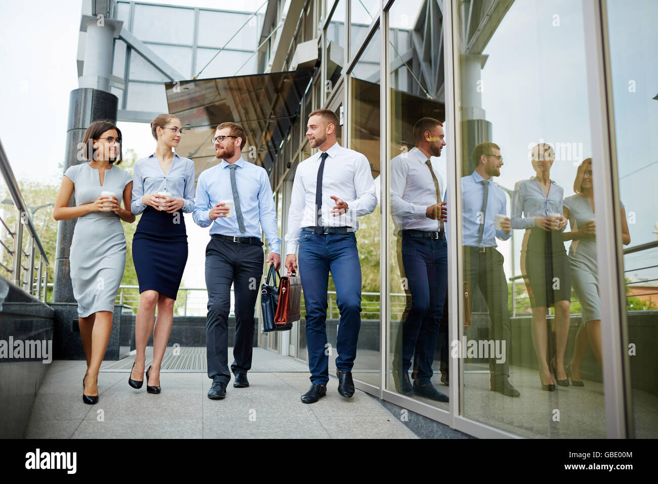 Group of managers with drinks walking along wall of office center and ...