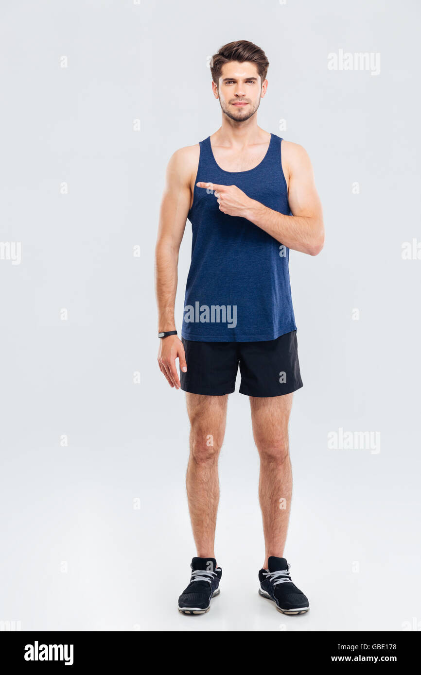 Young serious sportsman pointing finger at copyspace isolated on a gray ...