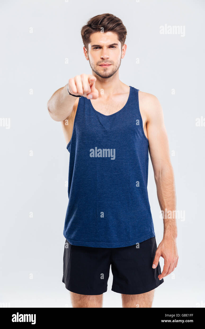 Confident young man athlete standing and pointing on you over white ...