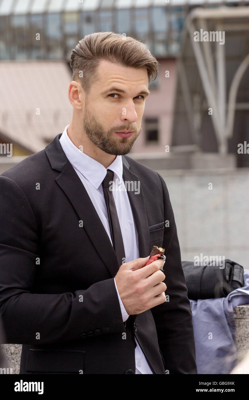 Young business man eating chocolate outdoors Stock Photo - Alamy