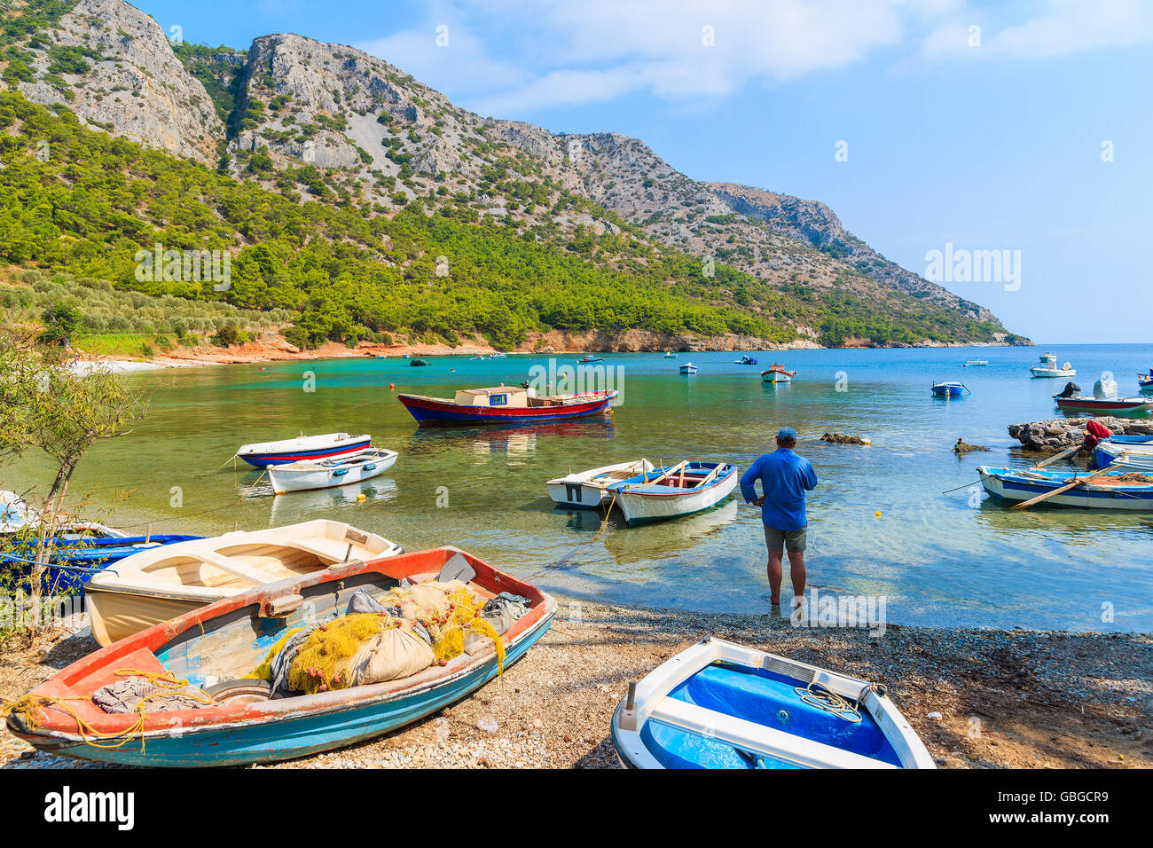 Fisherman standing among fishing boats on secluded beach, Samos island ...