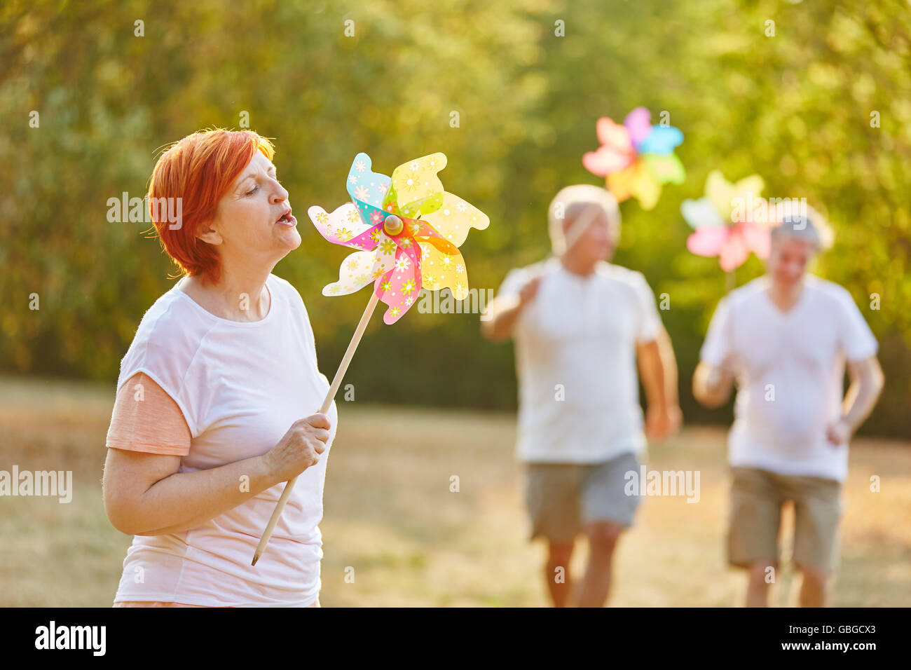 Senior woman holding a windmill and blowing Stock Photo - Alamy