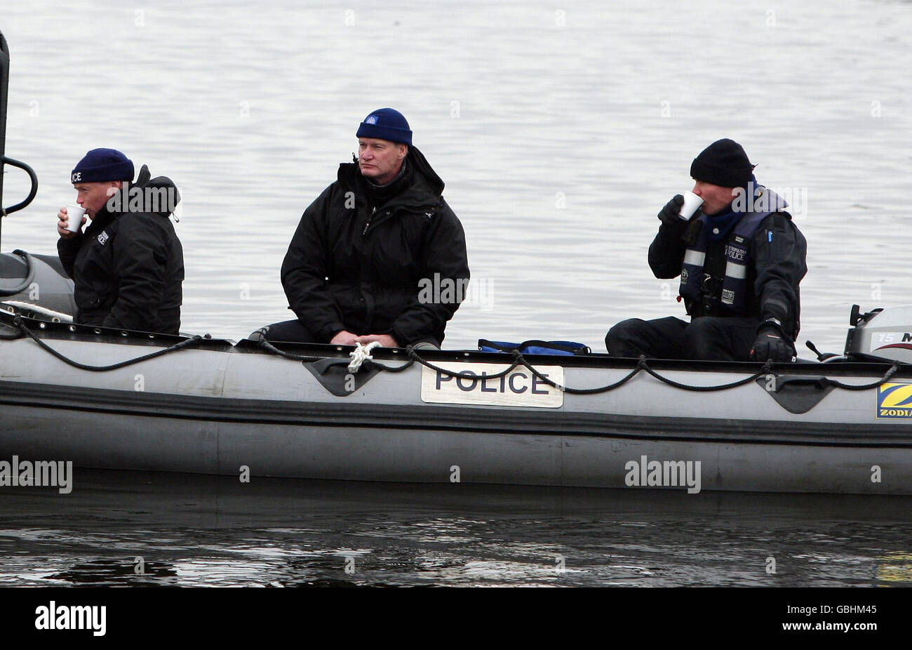 Police officers in a boat have a drink as they patrol the dock area ...