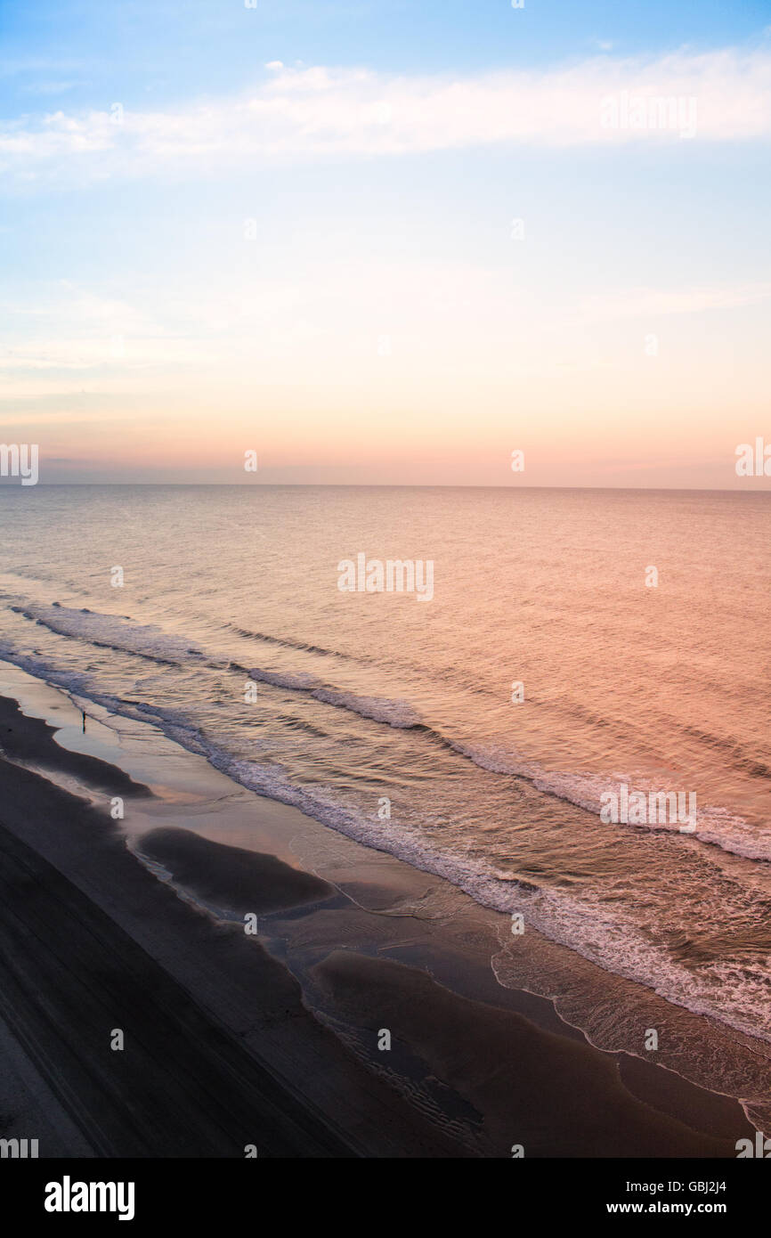 A colorful sunrise on the shoreline of a beach with a surf fisherman ...