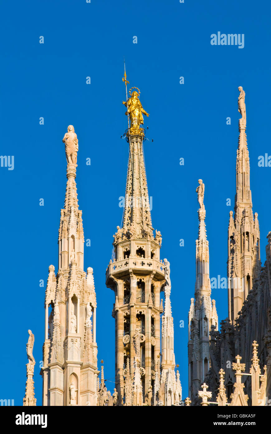Madonnina statue on cathedral spire against blue sky, Milan city, Italy ...