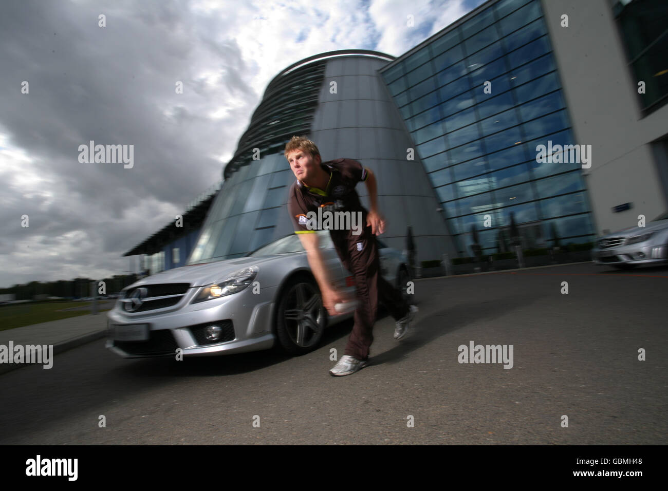 Surrey's Stuart Meaker bowls in front of a Mercedes AMG car alongside ...