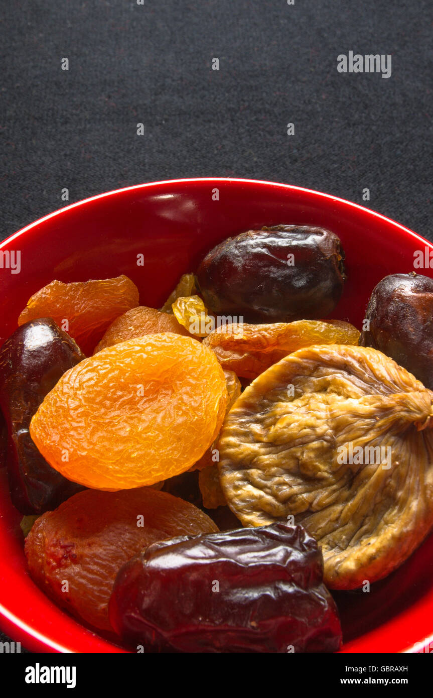 various dried fruits in red plate on black background Stock Photo - Alamy