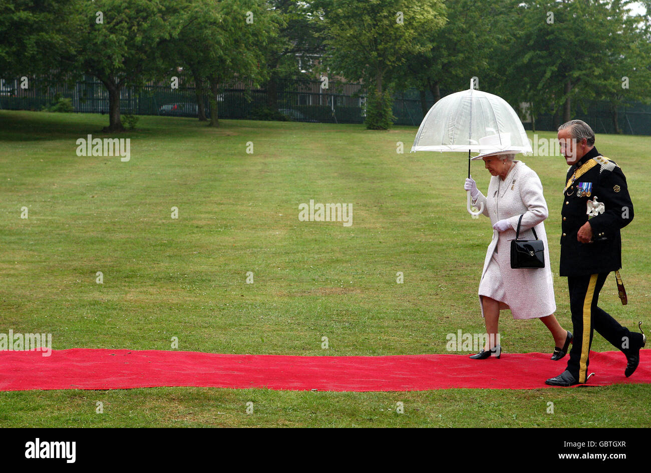 Queen Elizabeth II walks across a red carpet laid on grass with ...