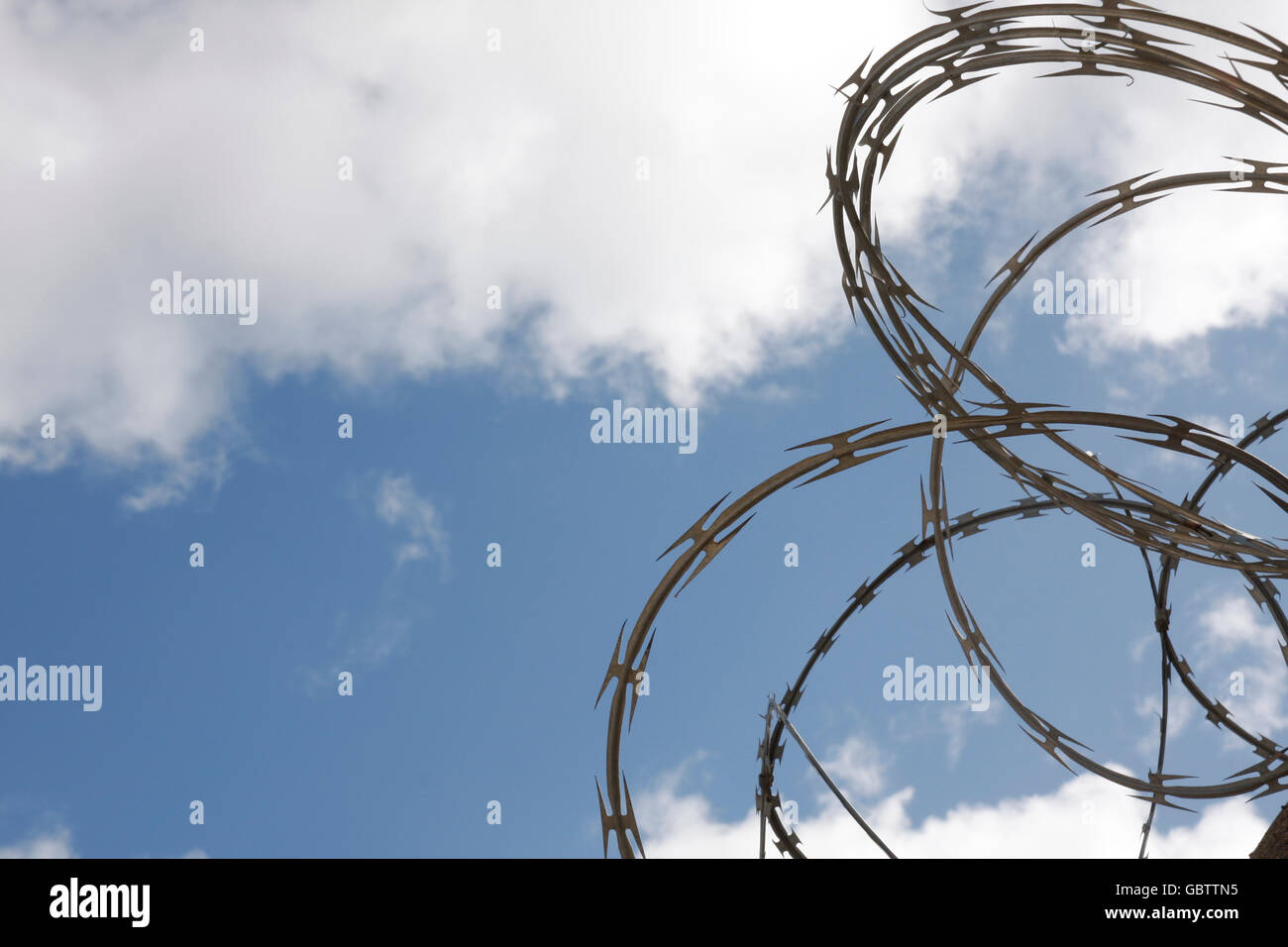 Razor wire against a blue sky with clouds Stock Photo - Alamy