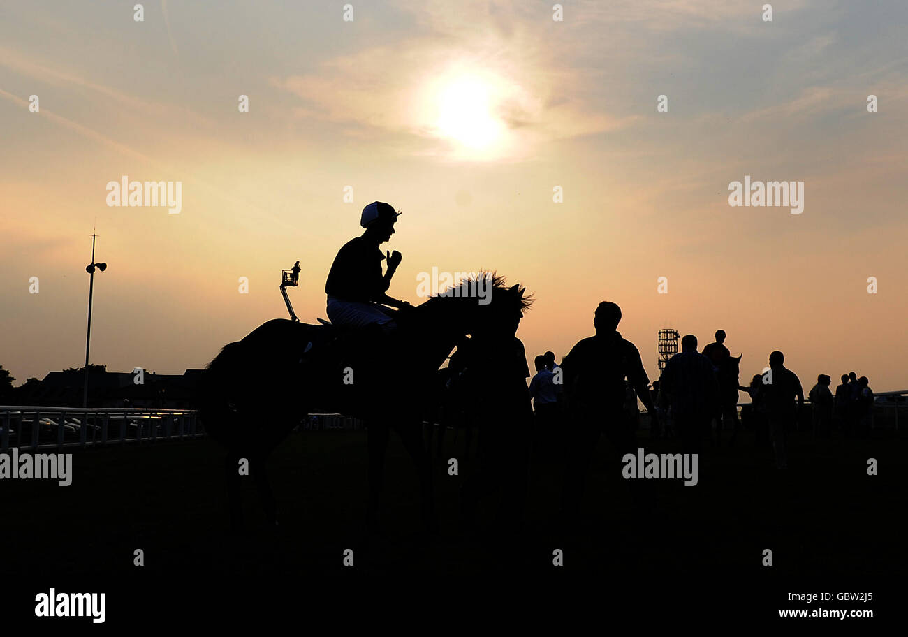 A jockey is lead off the course after his race as the sun sets behind ...
