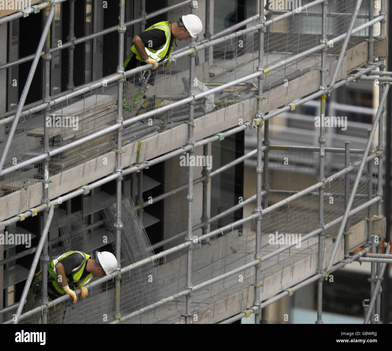 Two workers look over the side of scaffolding on the outside of a newly ...