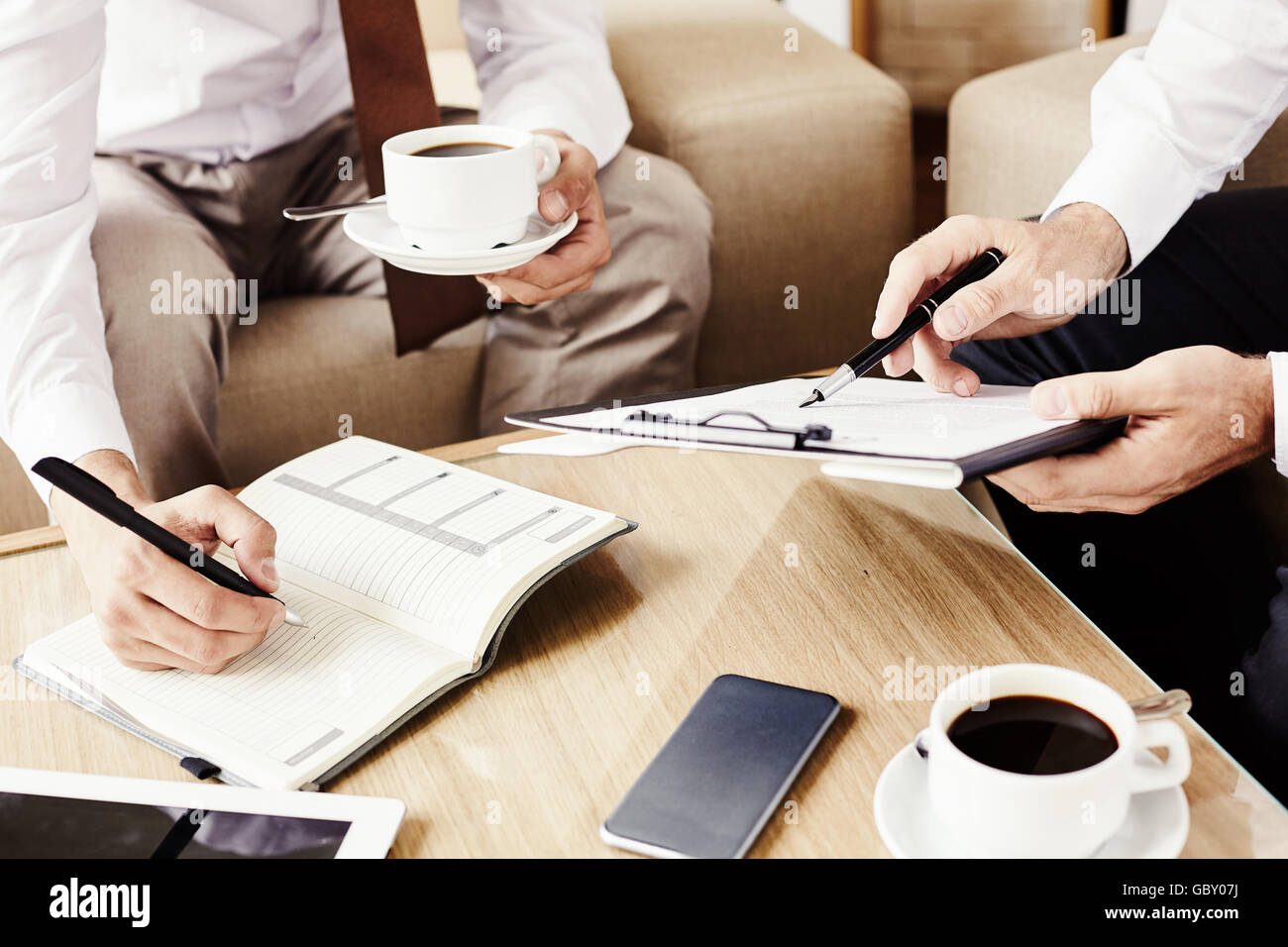 Two colleagues signing documents while drinking coffee Stock Photo - Alamy
