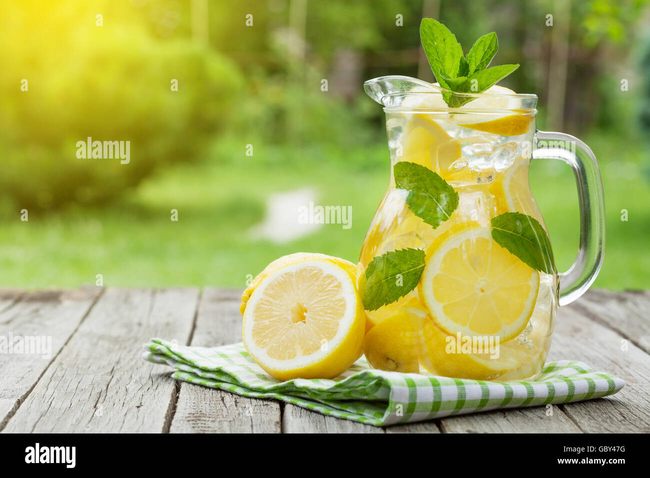 Lemonade pitcher with lemon, mint and ice on garden table. View with ...