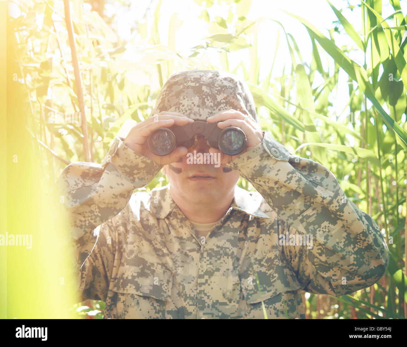 A soldier man is looking through binoculars in the woods outside with a ...
