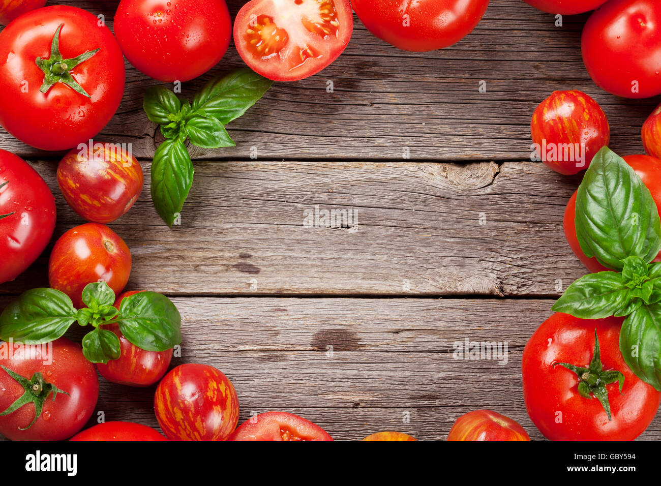 Fresh ripe garden tomatoes and basil on wooden table. Top view with ...