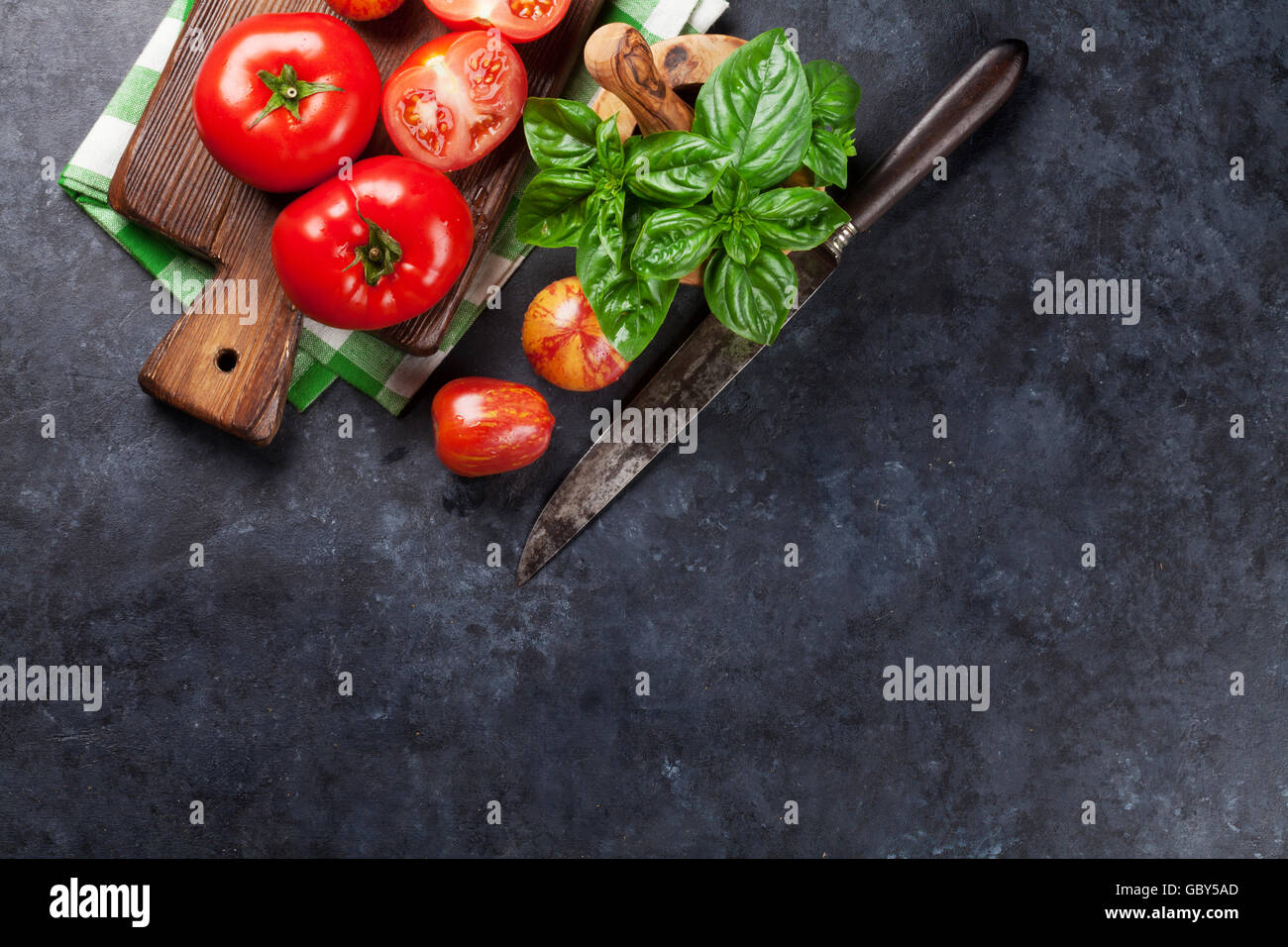 Fresh ripe garden tomatoes and basil on stone table. Top view with copy ...
