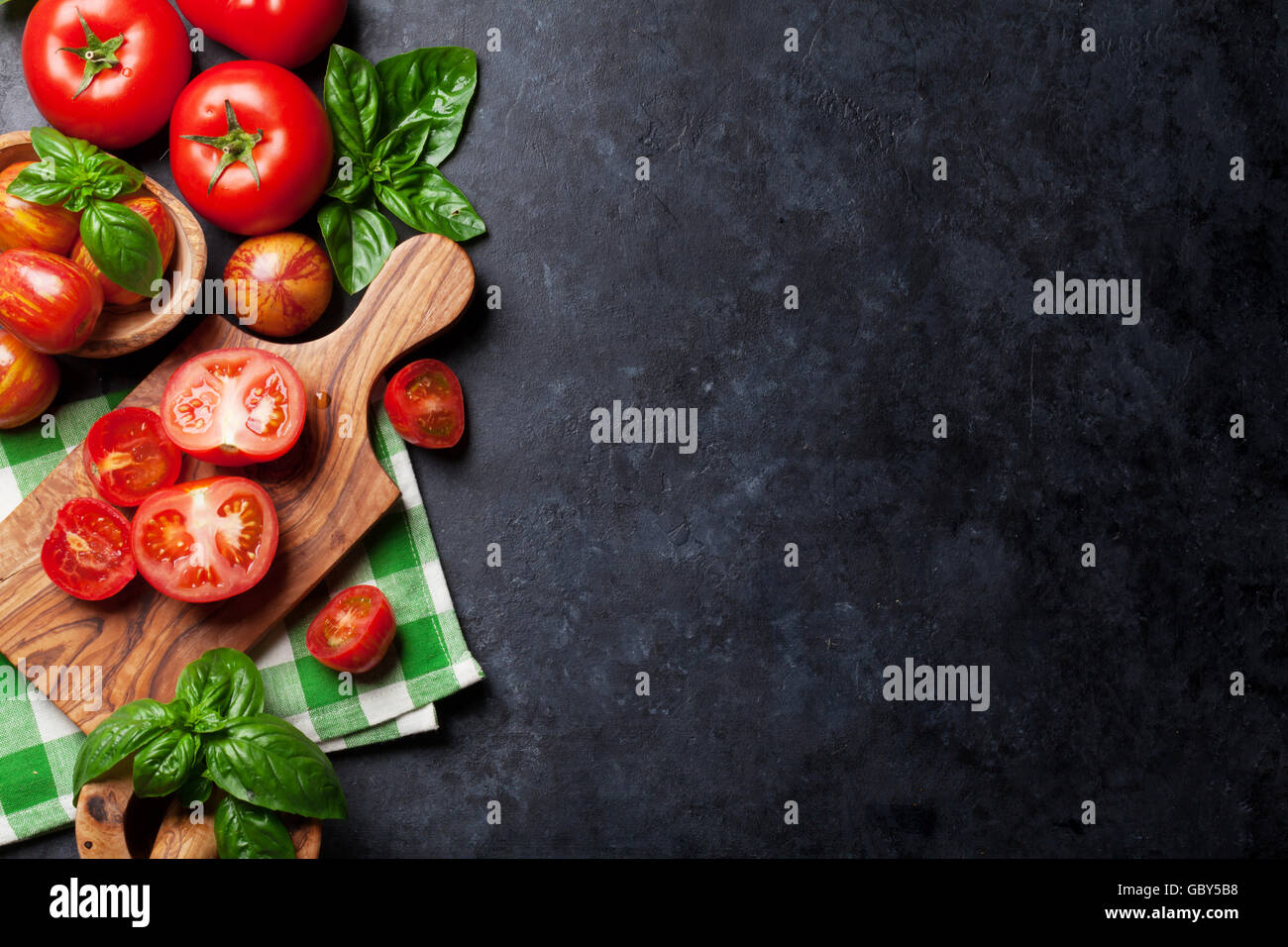 Fresh ripe garden tomatoes and basil on stone table. Top view with copy ...