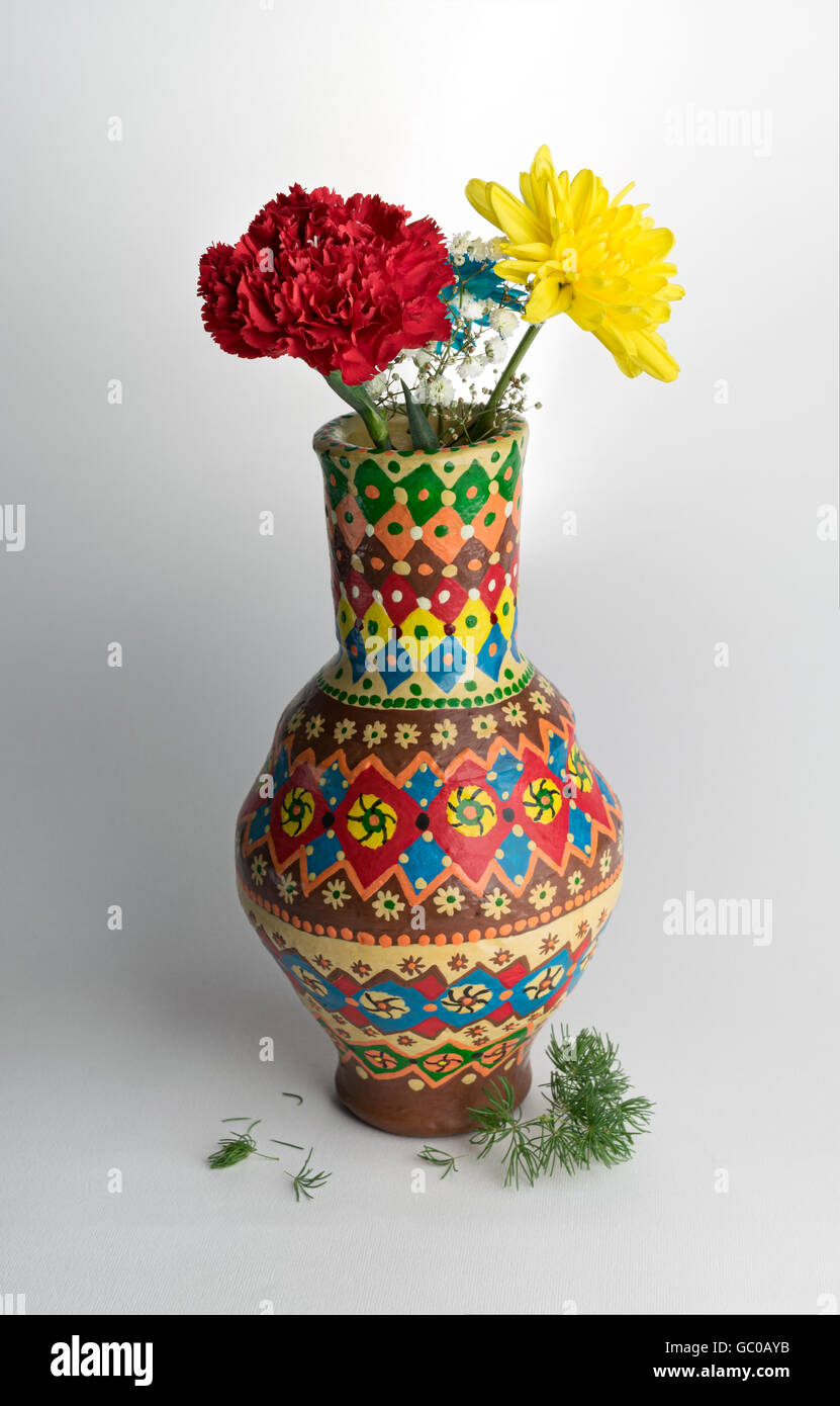 Still life composition of colorful pottery vase with two red and yellow flowers on white ...