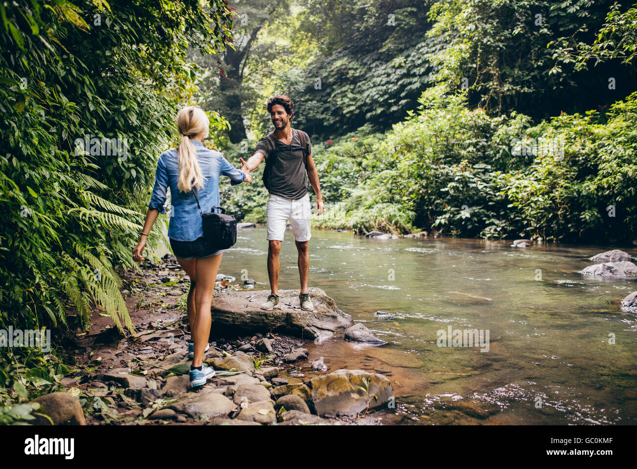 Young couple walking by the mountain stream with man helping his ...