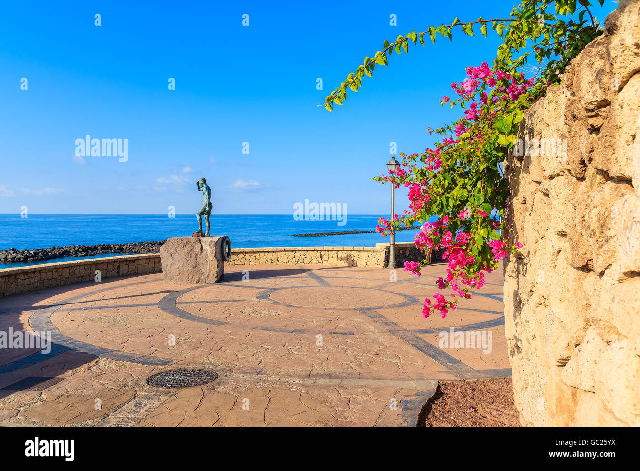 Coastal promenade with flowers and statue in Costa Adeje seaside town, Tenerife, Canary Islands ...