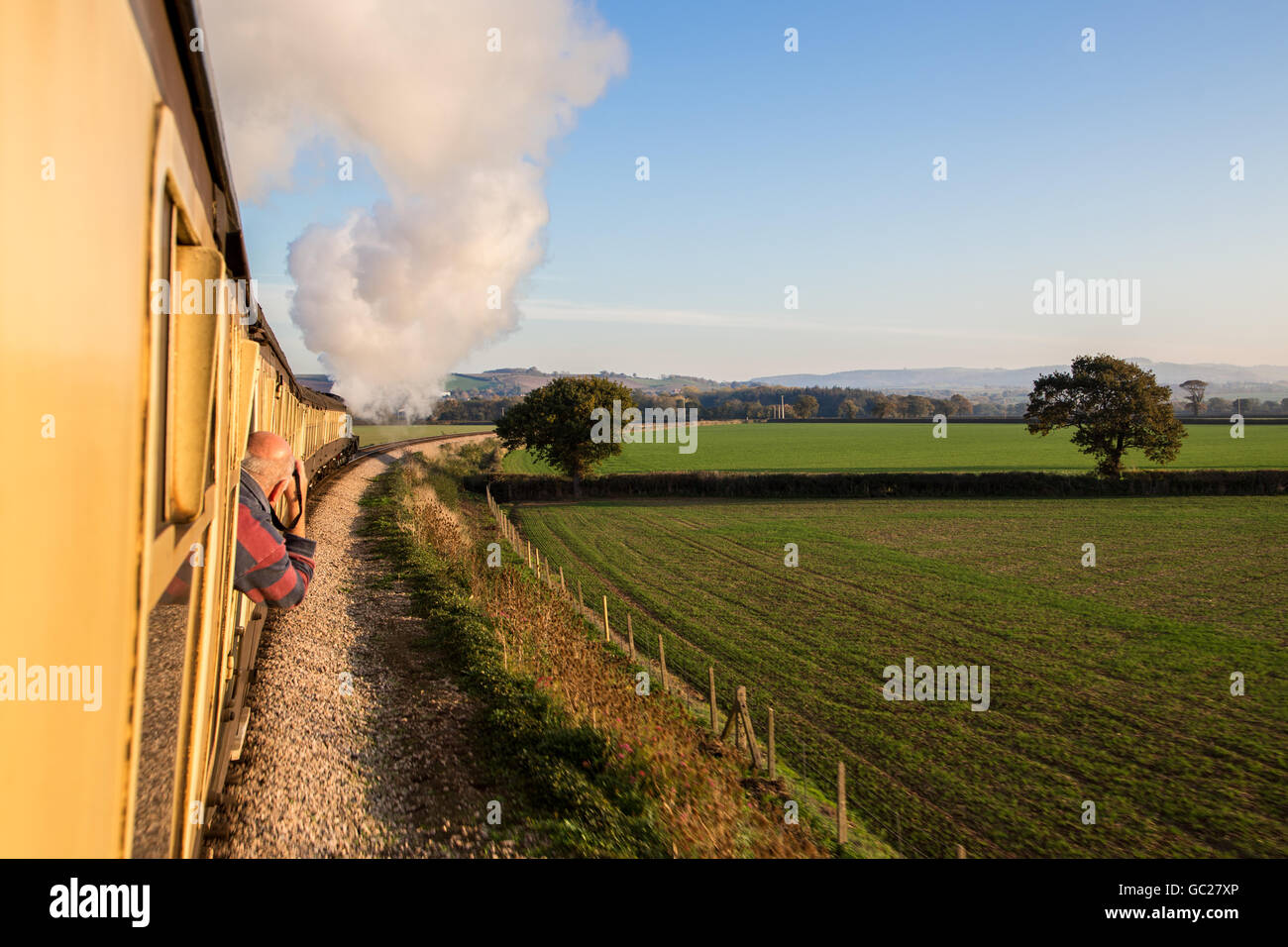 A man leans from a vintage steam train carriage window to take a ...