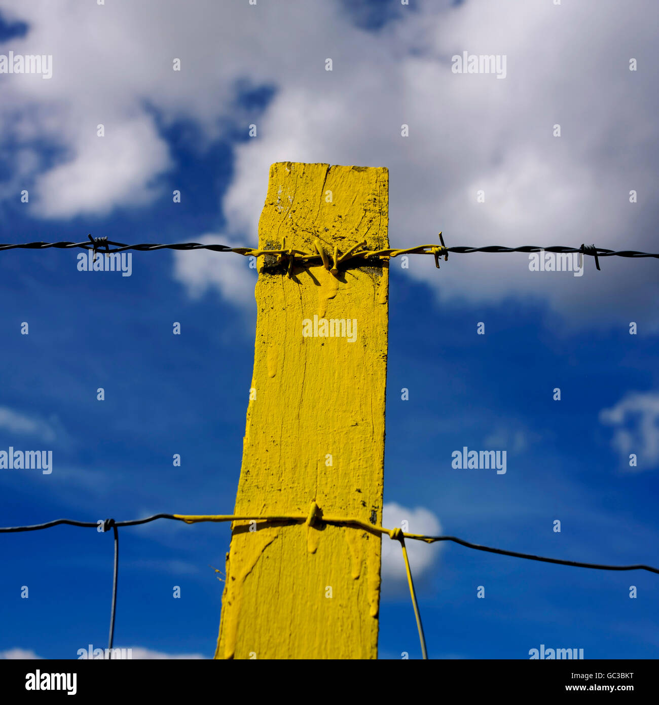 Yellow post, barbed wire, against blue sky with clouds Stock Photo - Alamy