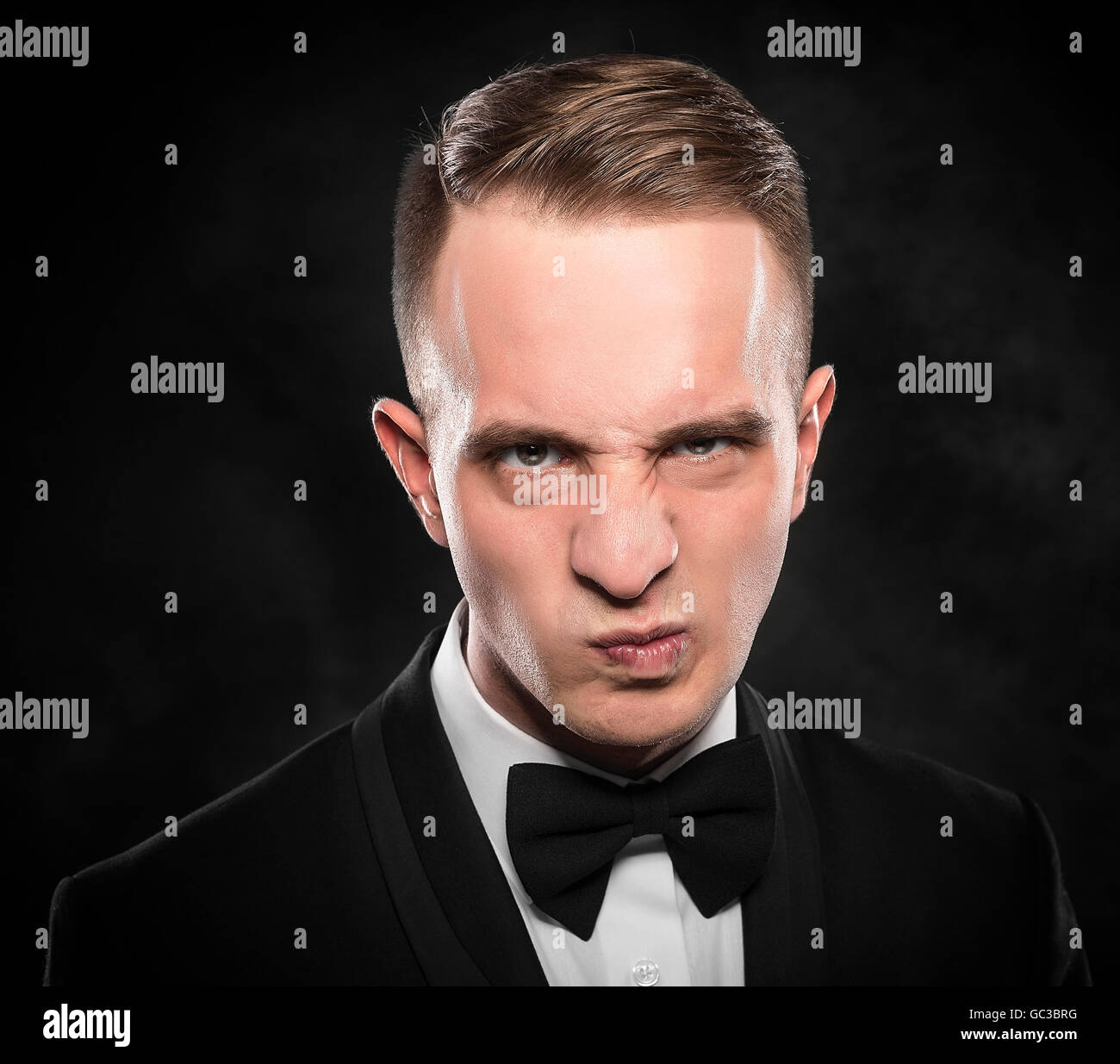 Elegant angry young man in suit looking frowning on dark background ...