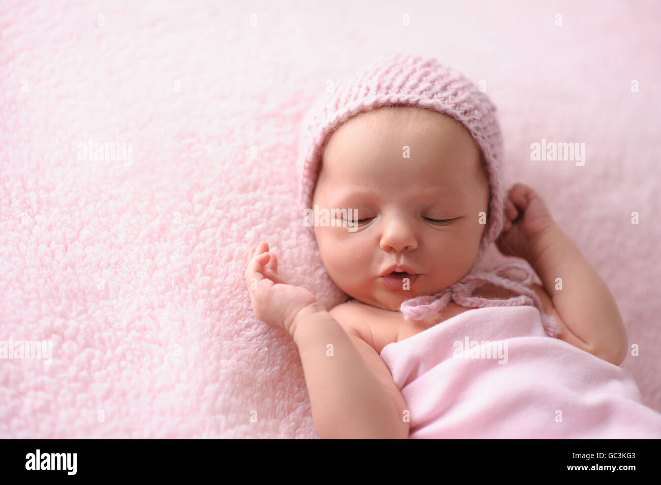 Portrait of a cooing, two week old, newborn baby girl. She is wearing a ...