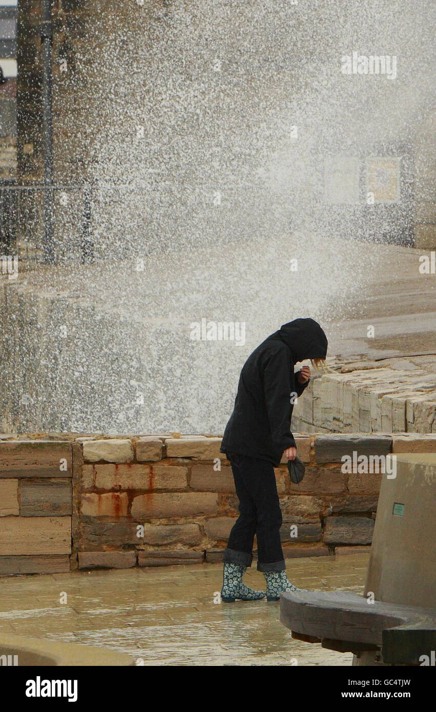 A walker attempts to dodge waves breaking over the sea wall in Old ...