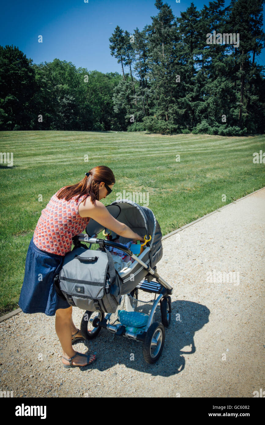 Mother looks into the pram on walk in the park. Rear view Stock Photo ...