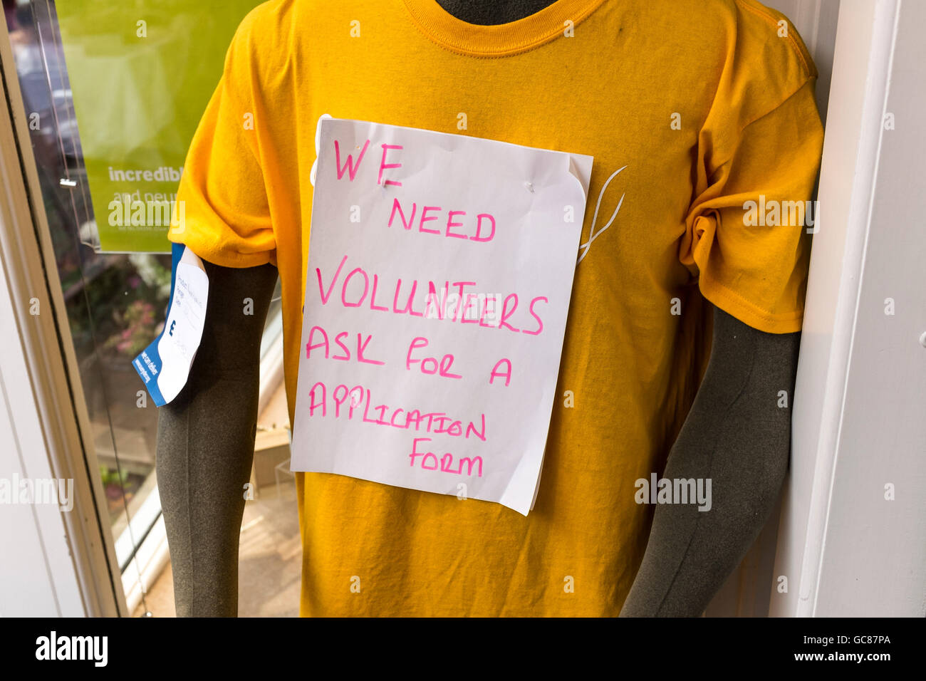 A handwritten sign asking for volunteers in a charity shop window ...