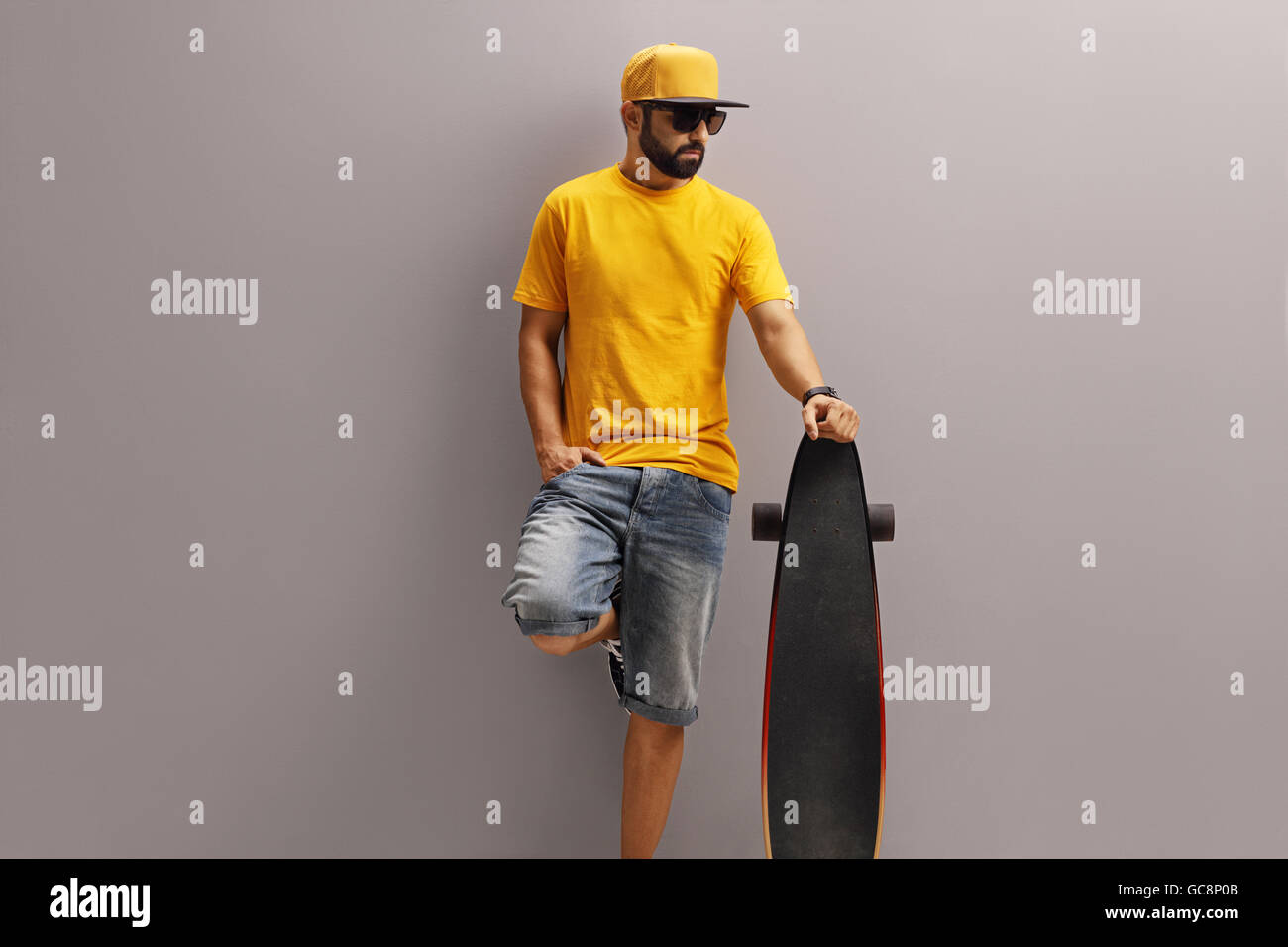 Cool young guy with yellow shirt and cap leaning against a wall and ...