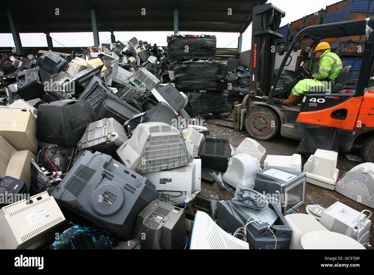 A folk-lift truck prepares to lift pallets of old television sets and ...