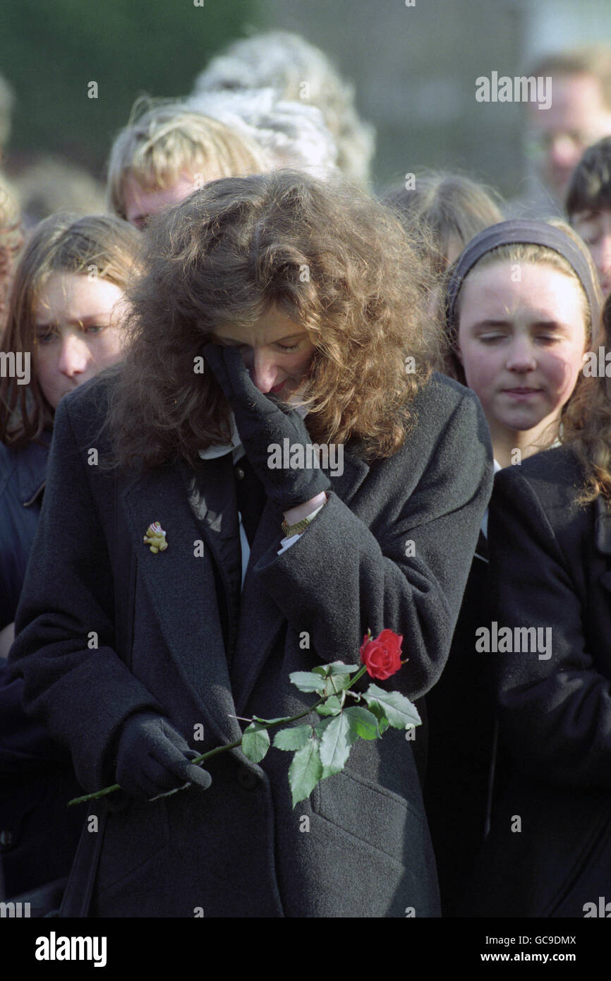 A MOURNER WIPES AWAY A TEAR AS SHE CARRIES A SINGLE RED ROSE BY THE ...