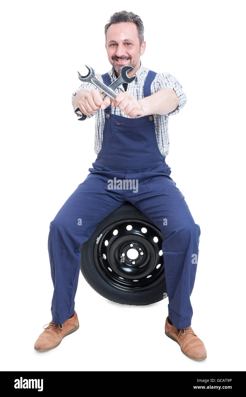 Smiling handsome mechanic with wrench sitting on tire as auto services ...