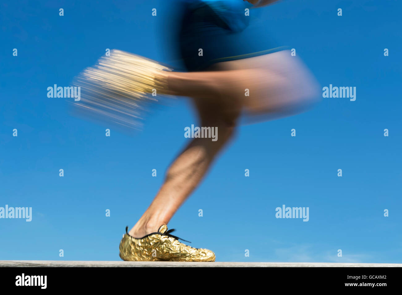 Athlete wearing gold running shoes runs past in a blur against bright ...