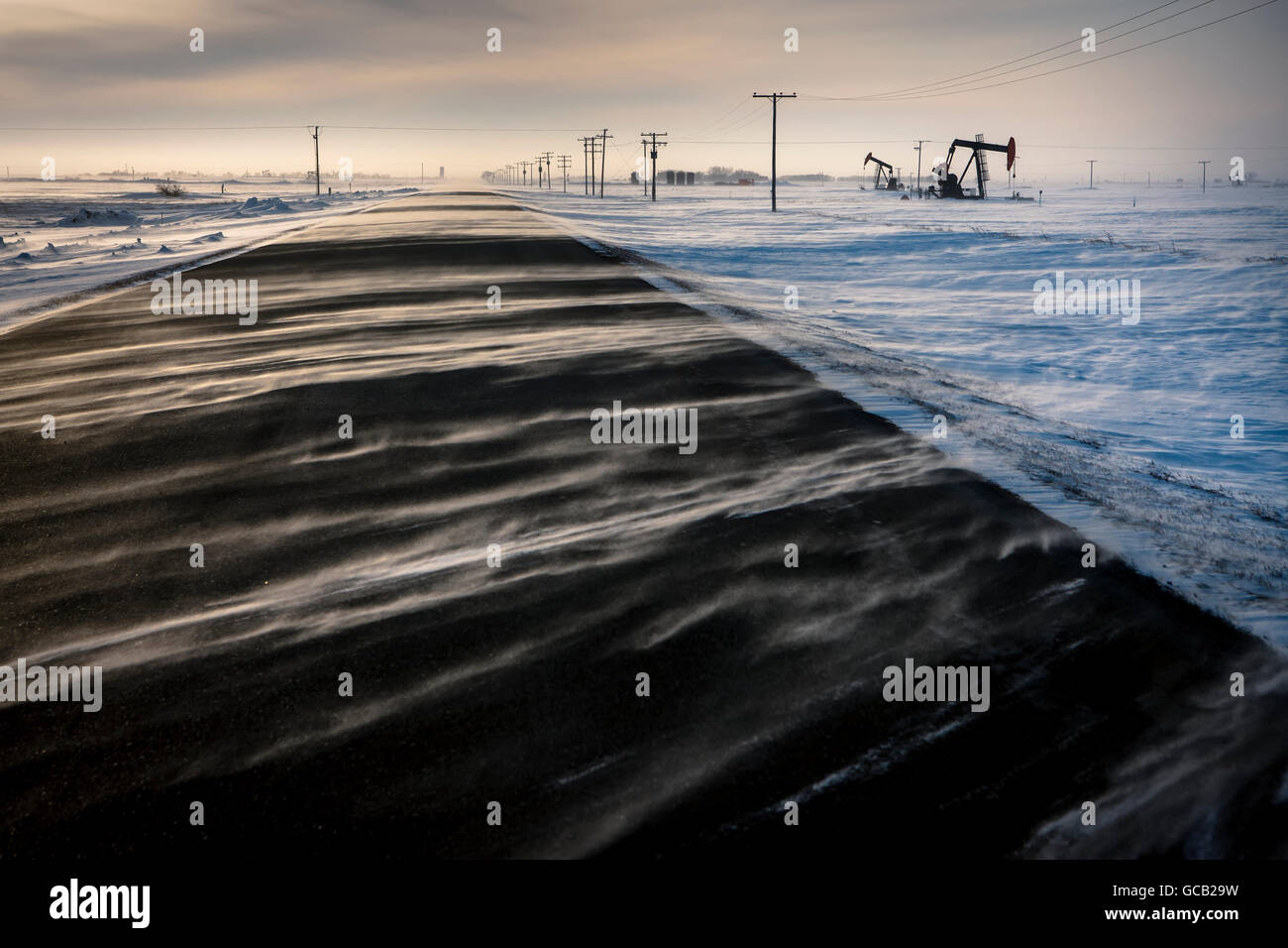 Snow blowing across the road in the prairies with oil well and pump ...