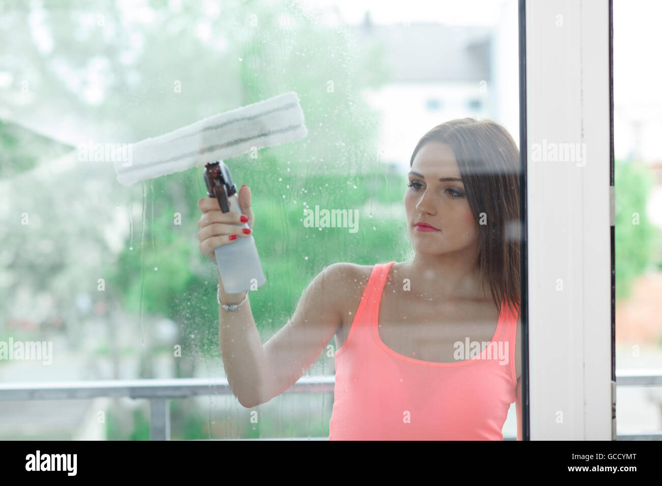 Beautiful young woman cleans a home. The girl washes the windows with a ...
