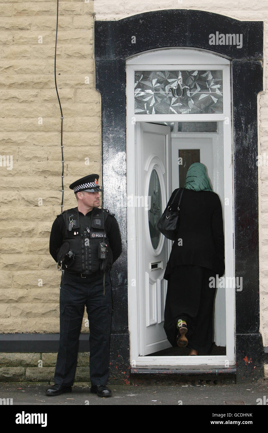 A woman enters the front door as a police officer stands outside the ...
