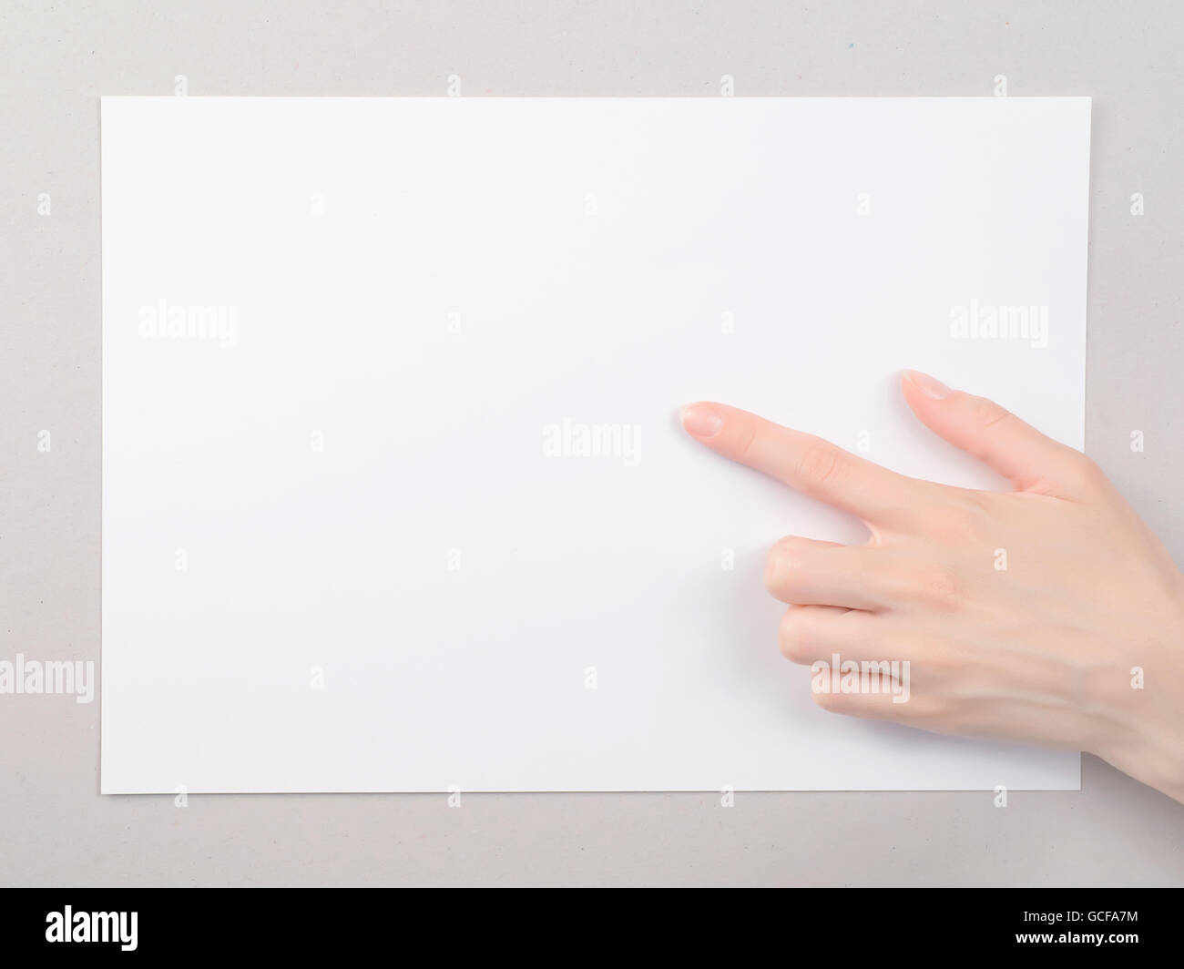 Woman`s finger pointing at the blank paper sheet. On gray cardboard ...