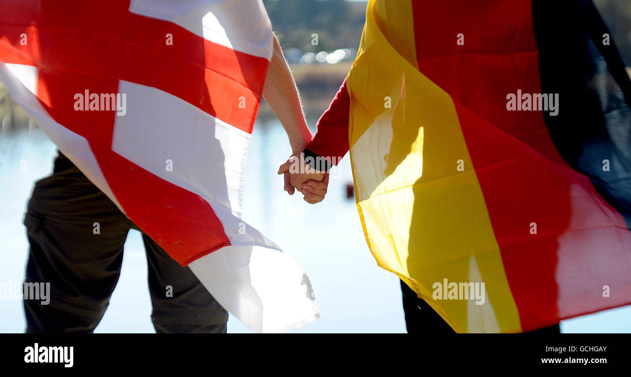 A couple wearing English and German flags hold hands beside a lake ...