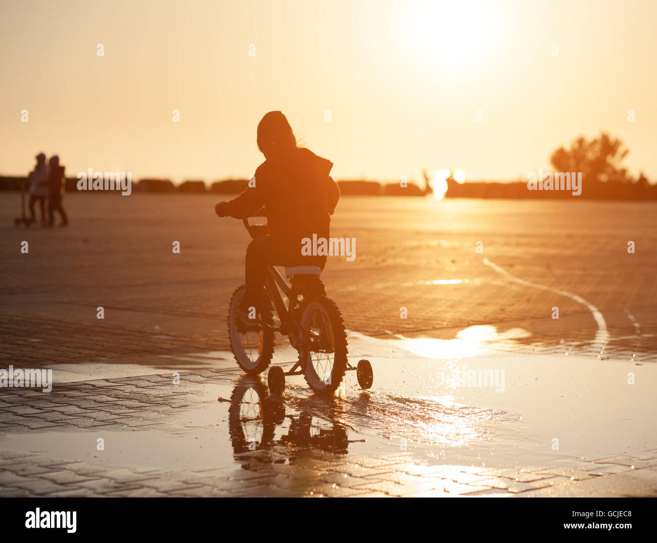 child rides a bicycle through a puddle on the background of the setting ...