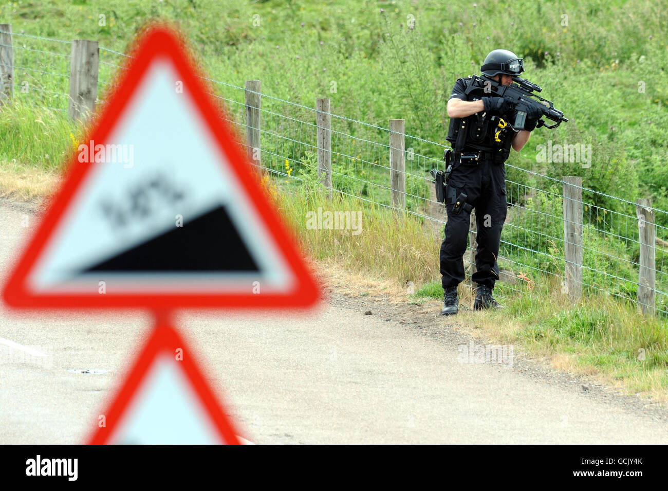 An arrmed police officer searches a field in countryside outside ...