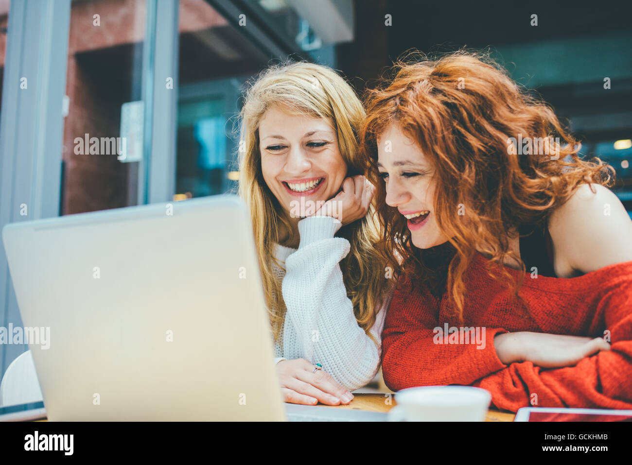 Two young beautiful caucasian blonde and redhead women using computer ...